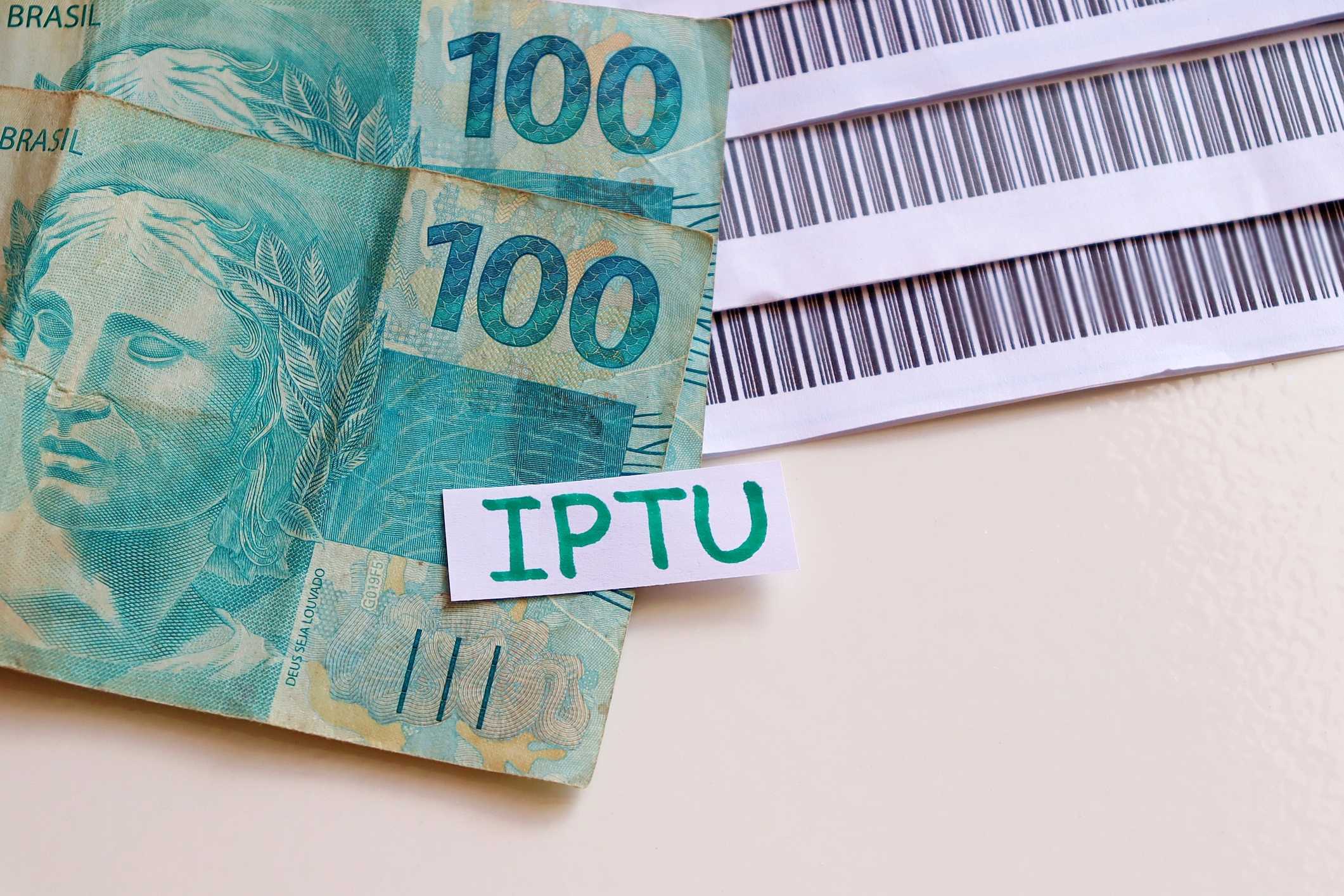 Três boletos e duas cédulas de 100 reais estão sob uma mesa branca, com ...